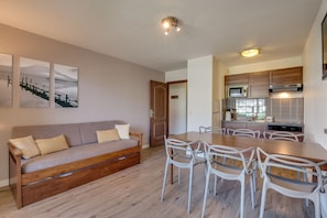 Uma sala de estar moderna com sofá, mesa de jantar e cadeiras. Há uma área de cozinha com micro-ondas e armários.