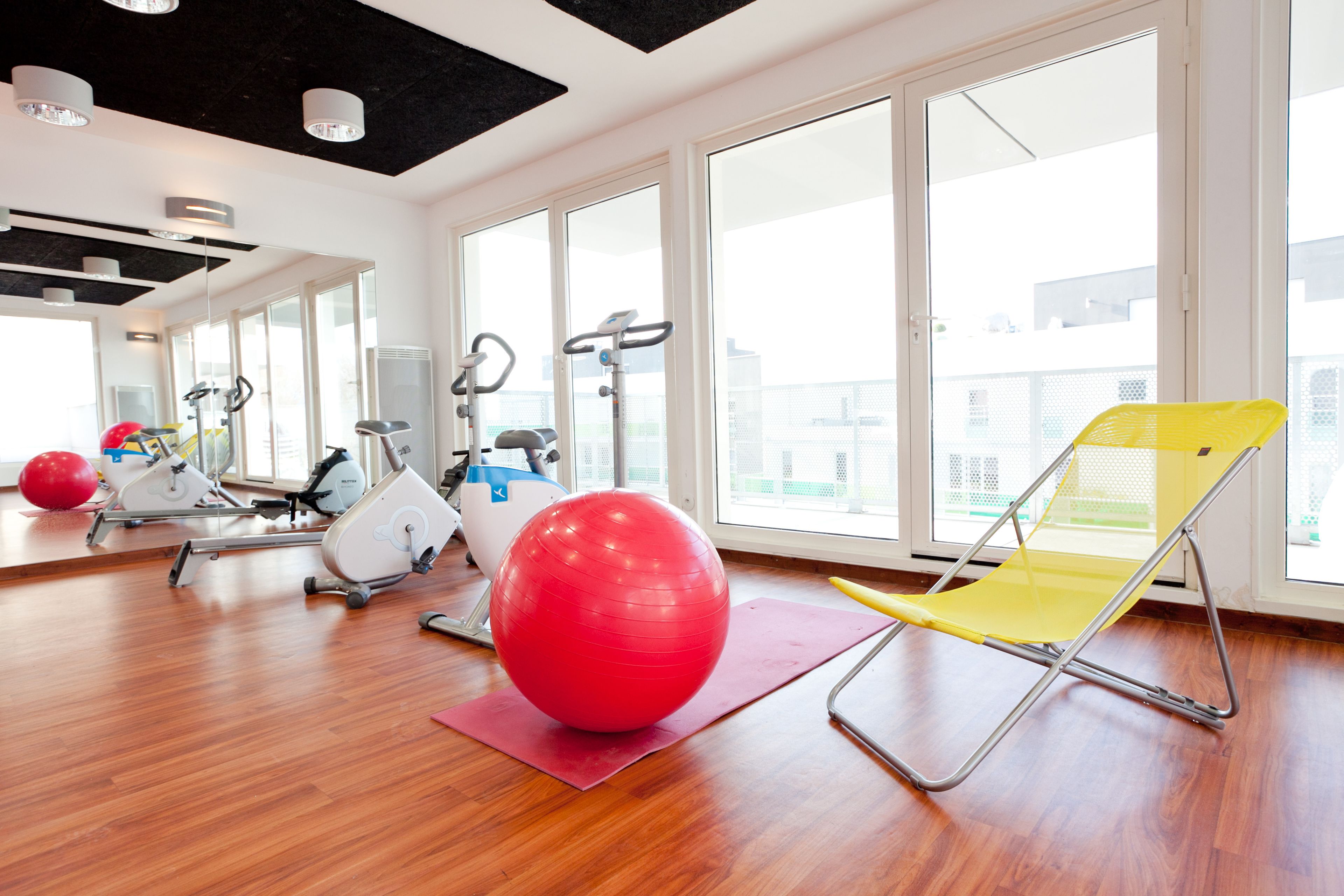 Uma academia com equipamentos de exercícios, uma bola de ginástica vermelha e uma cadeira amarela.