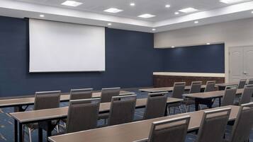 Uma sala de conferências com mesas, cadeiras, tela de projeção e um palanque.