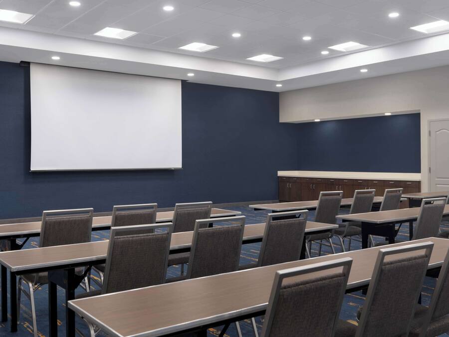 Uma sala de conferências com mesas, cadeiras, tela de projeção e um palanque.