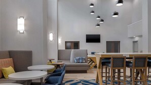 Um lobby de hotel moderno com um sofá, mesas redondas e uma área de refeições com cadeiras.