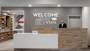 Balcão de recepção de hotel com uma placa que diz "WELCOME TO THE BIG SKYSTATE" e uma placa "Hilton Honors" logo abaixo.