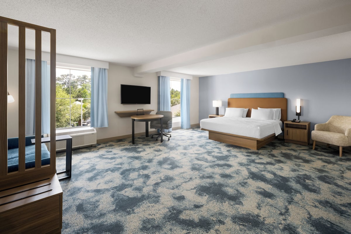 Quarto de hotel com cama, escrivaninha, cadeira, televisão e vista para o exterior.