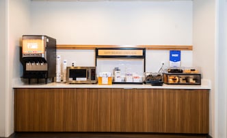 Um balcão de café da manhã com máquina de café, micro-ondas e vitrine de produtos de panificação.