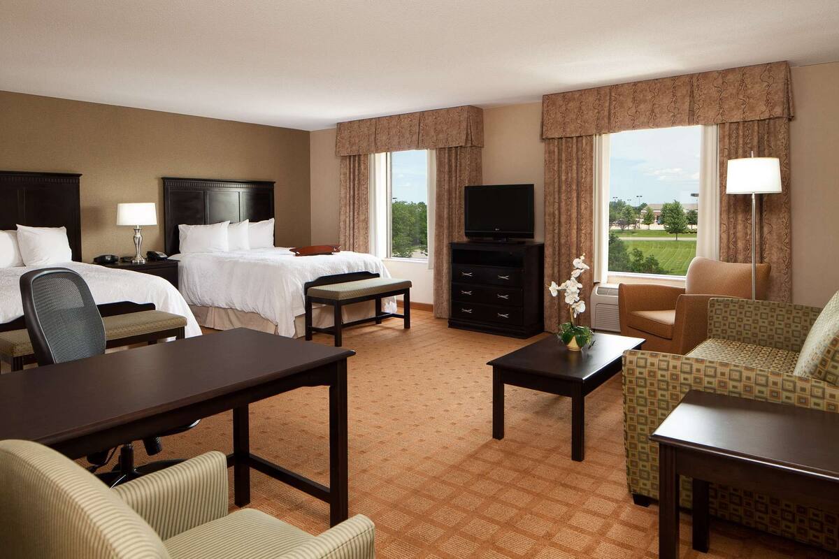 Quarto de hotel com duas camas, televisão, escrivaninha, cadeira e sofá.