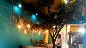 Uma área de recepção com espaço para sentar, uma árvore com luzes penduradas e uma pessoa em pé.