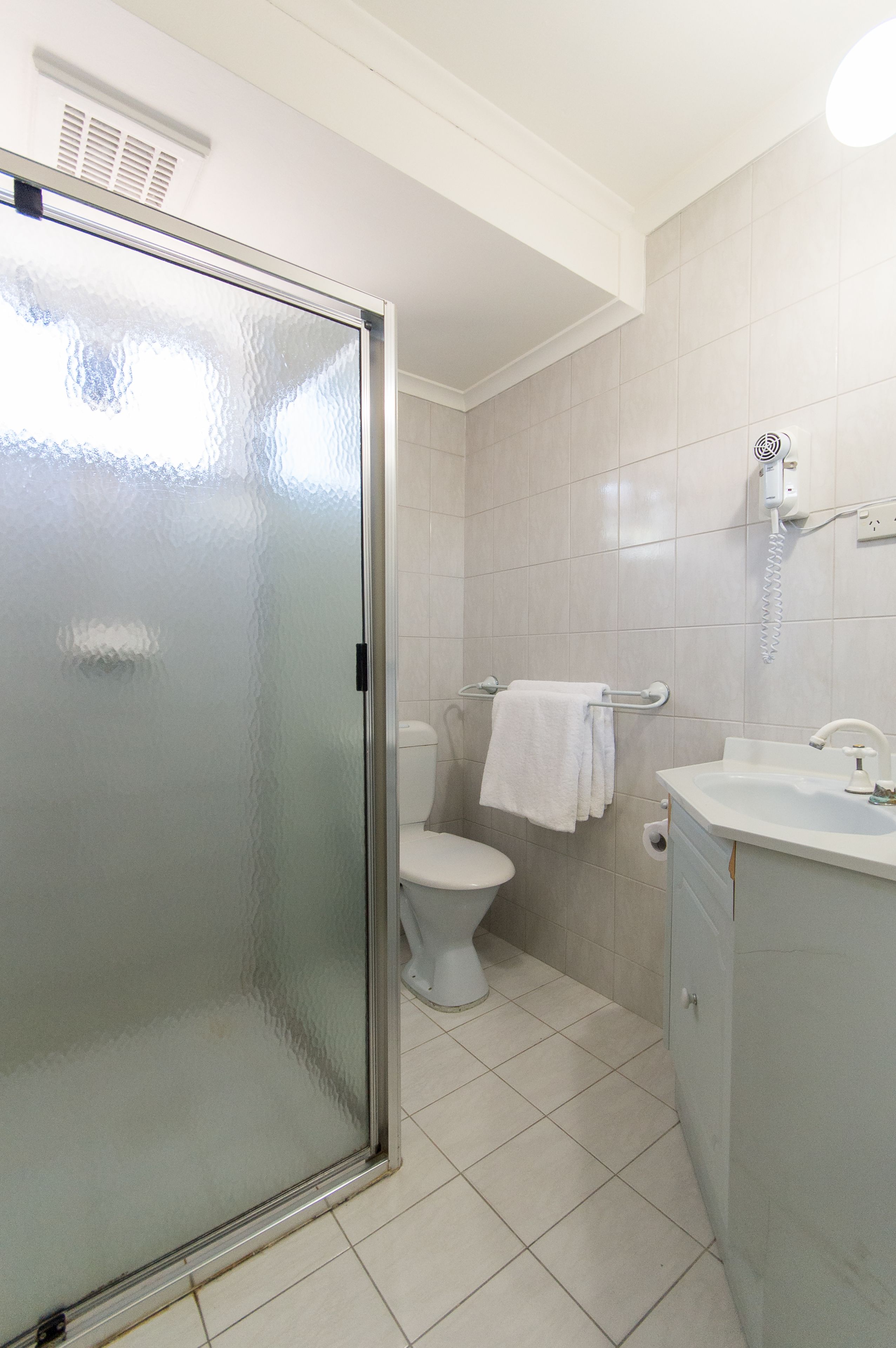Casa de banho com chuveiro de porta de vidro, sanita, lavatório e um porta-toalhas.