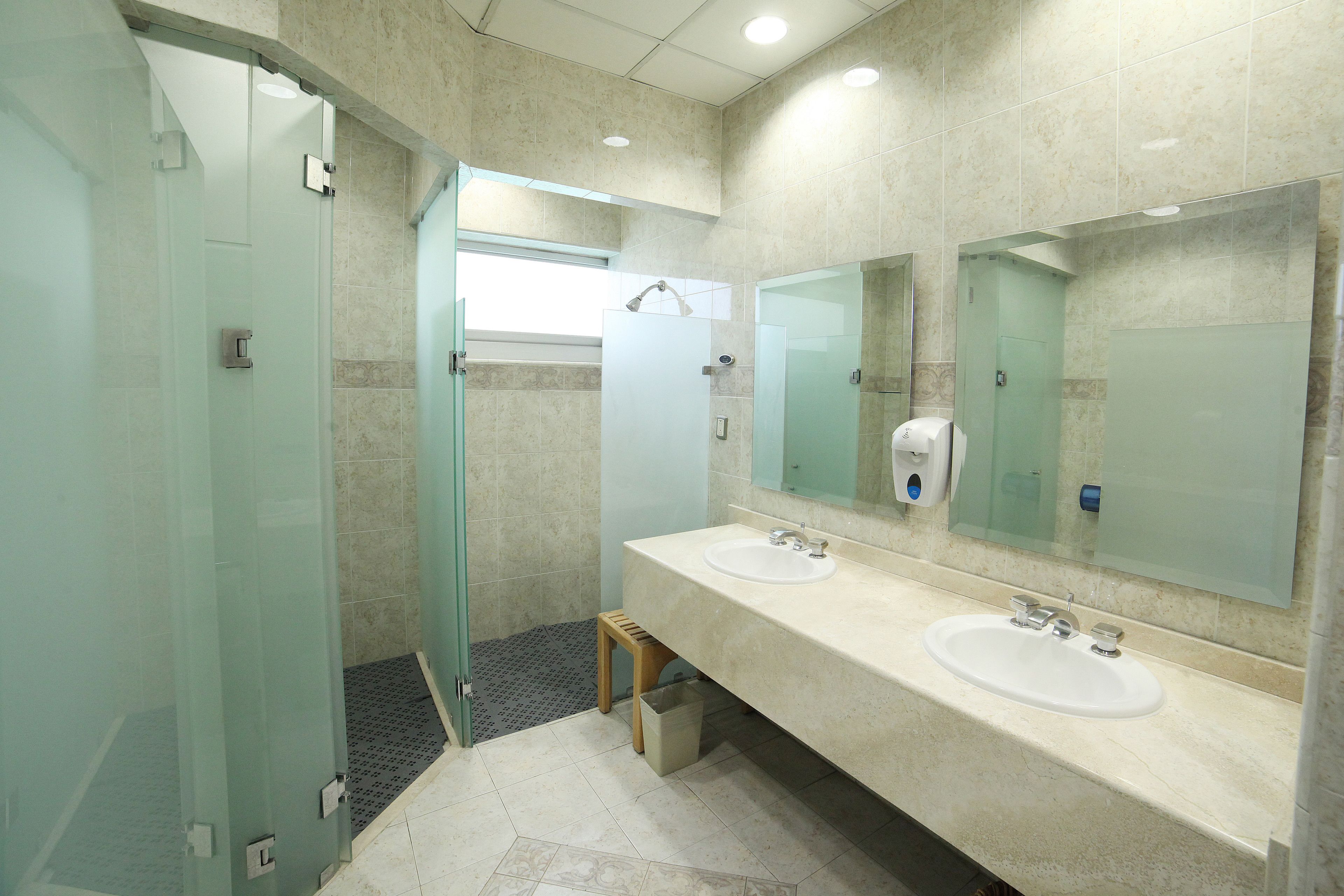 Casa de banho moderna com duas pias, cabine de duche em vidro e um pequeno banquinho.