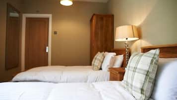 Quarto de hotel com duas camas de solteiro, cabeceira de madeira, abajur e um espelho na parede.