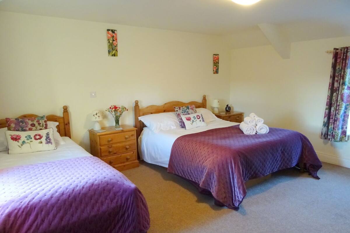 Quarto com duas camas de solteiro, cabeceiras de madeira, mesas de cabeceira com abajures e detalhes decorativos florais.