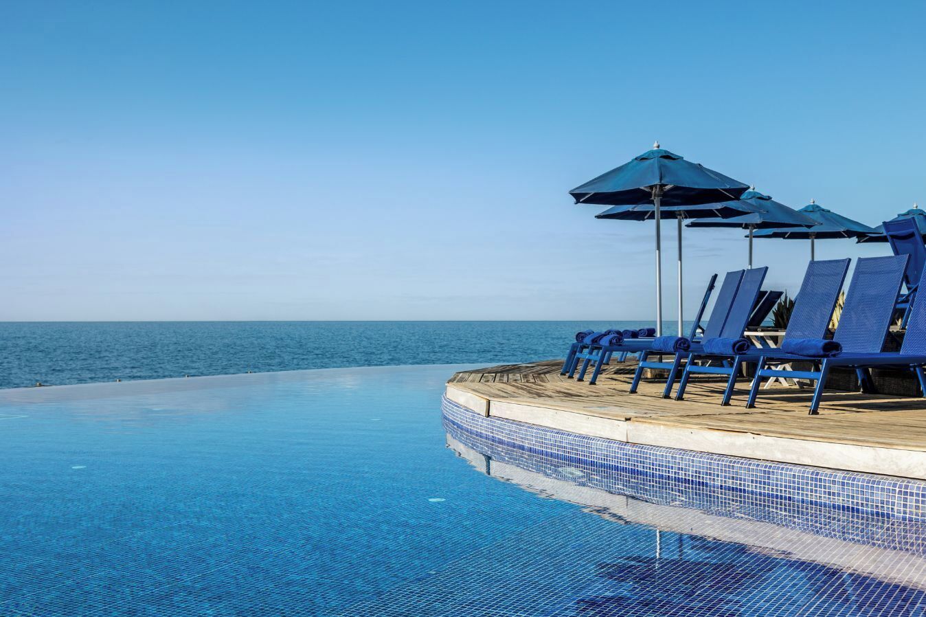 Piscina infinita com vista para o oceano, espreguiçadeiras e guarda-sóis.