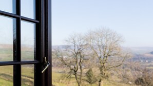 Janela com vista para uma paisagem rural, incluindo uma árvore e um edifício com telhado vermelho.