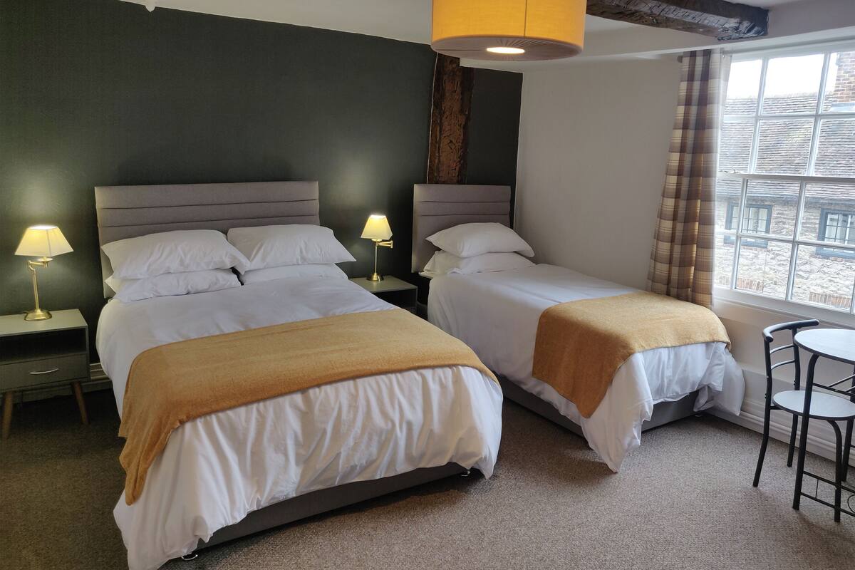 Quarto de hotel com duas camas, uma mesinha e janela com cortinas.
