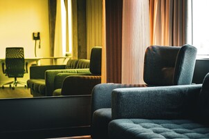 Quarto com um espelho grande, um sofá verde, uma poltrona azul e uma janela com cortinas.