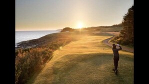 Uma pessoa em campo de golfe com vista para o oceano e o pôr do sol.