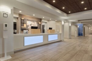Uma área de recepção de hotel com design moderno, incluindo um balcão de atendimento, um visor digital e um piso limpo revestido de azulejos.