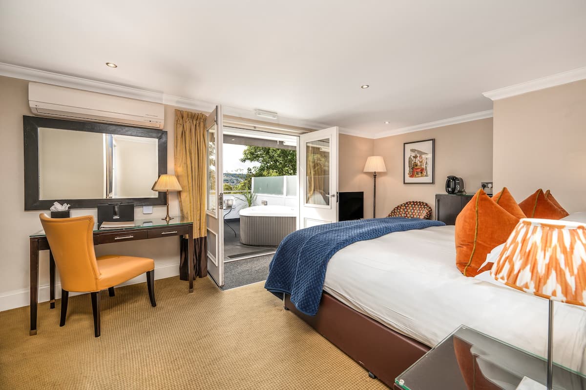 Quarto de hotel com cama, escrivaninha, cadeira, televisão e banheiro visível por uma porta aberta.