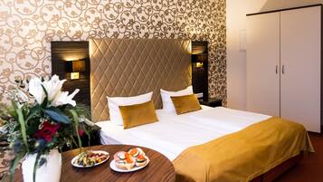 Quarto de hotel com uma cama grande, uma mesinha de cabeceira com um vaso de flores e uma travessa de frutas.