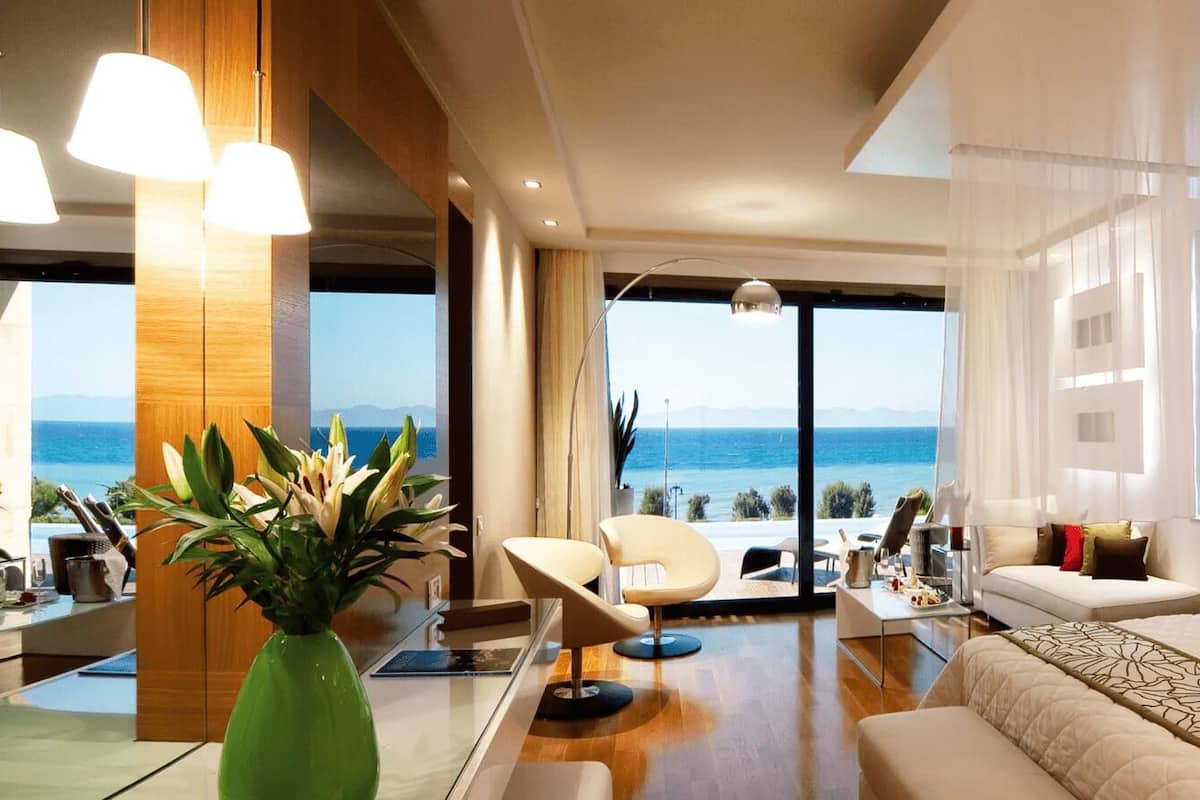 Uma sala de estar moderna com uma janela ampla vista para o mar, um sofá, um espaço de refeições e vista para o oceano.