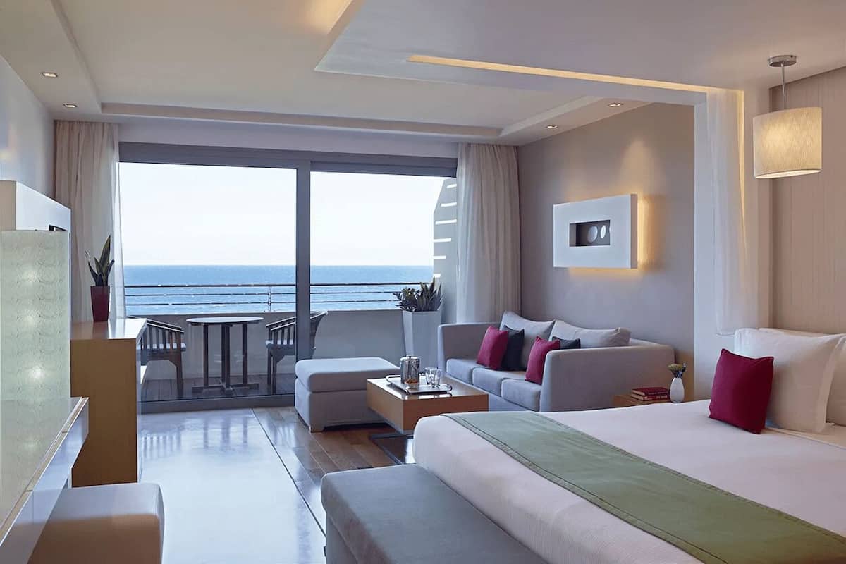 Quarto de hotel moderno com varanda, sofá, cama e mesa de centro.
