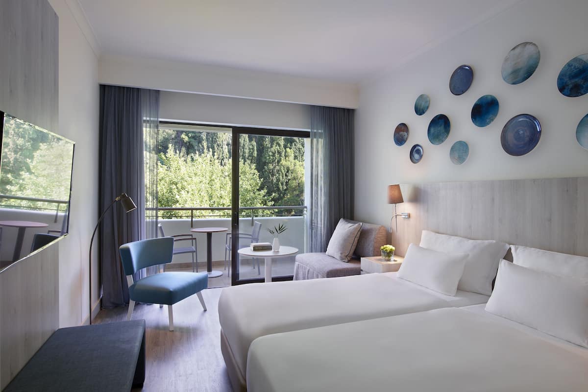 Quarto de hotel com uma cama grande, uma escrivaninha, uma cadeira e varanda com vista para árvores.