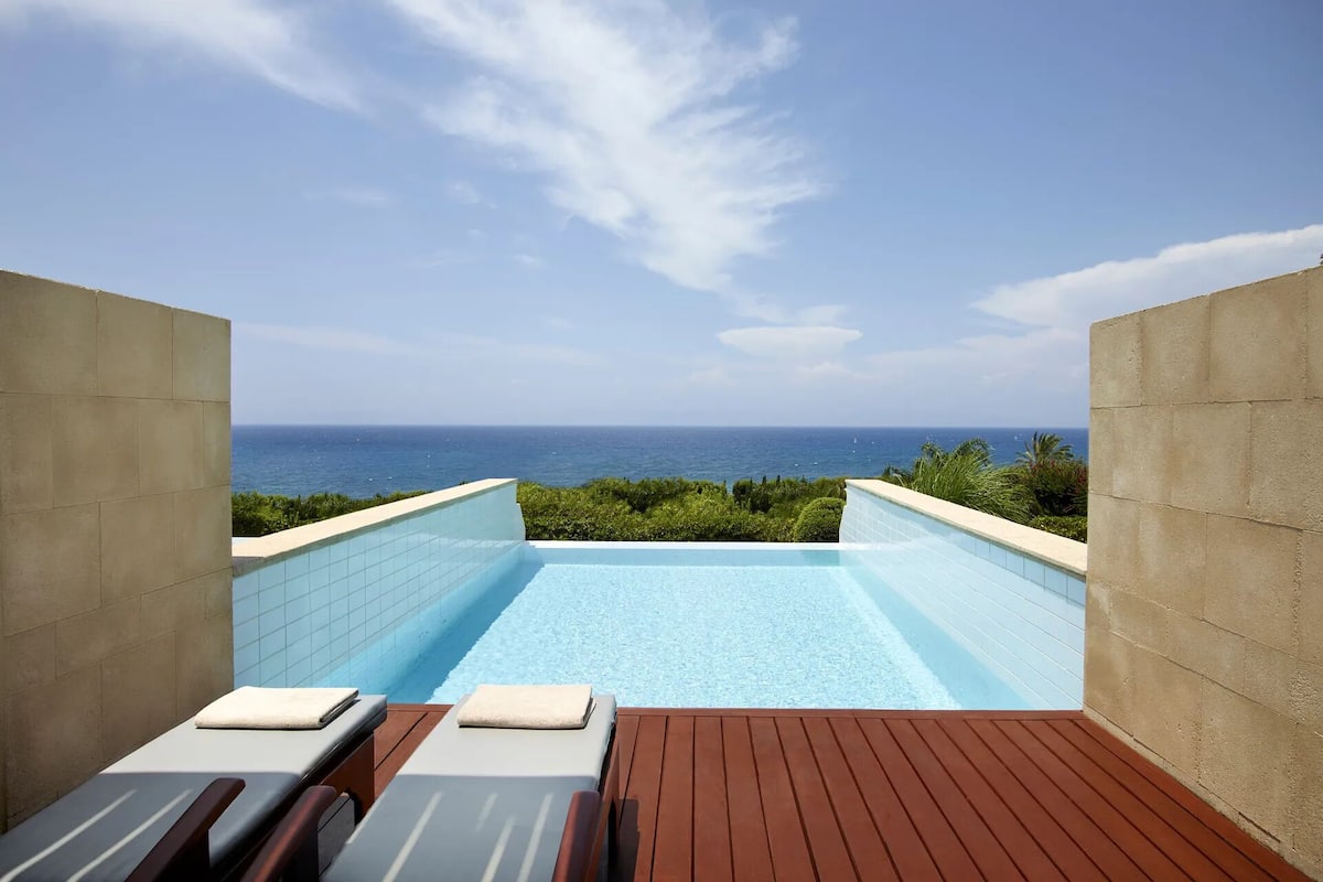 Piscina infinita no terraço com deck de madeira e espreguiçadeiras, com vista para o oceano.