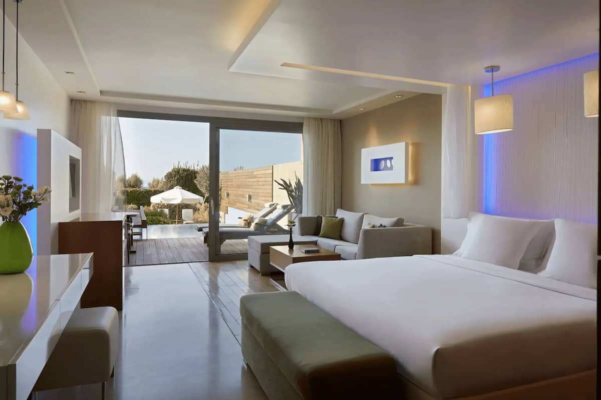 Quarto de hotel moderno com uma cama grande, uma escrivaninha e um espaço de estar com vista para o exterior.