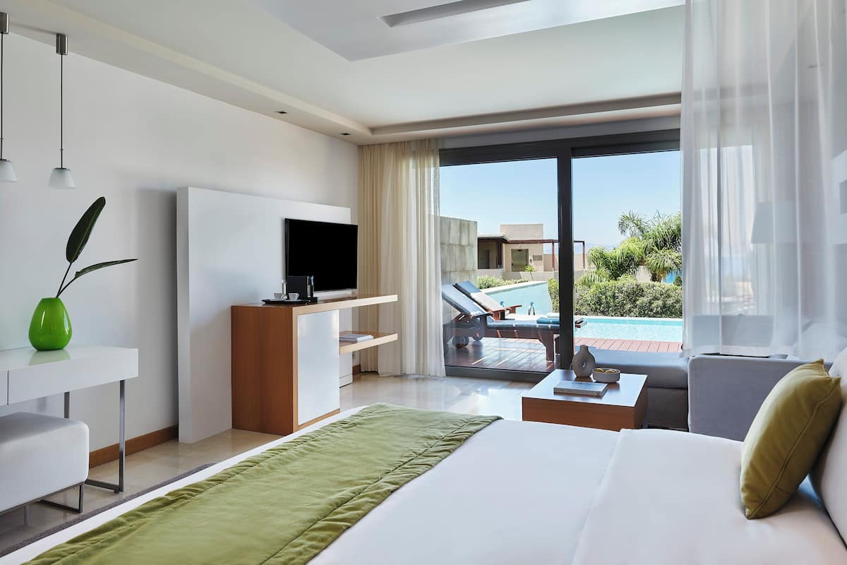 Quarto de hotel moderno com cama, TV, escrivaninha e vista para uma piscina ao ar livre.