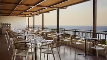 Restaurante com mesas ao ar livre e cadeiras de vime, com vista para o mar.