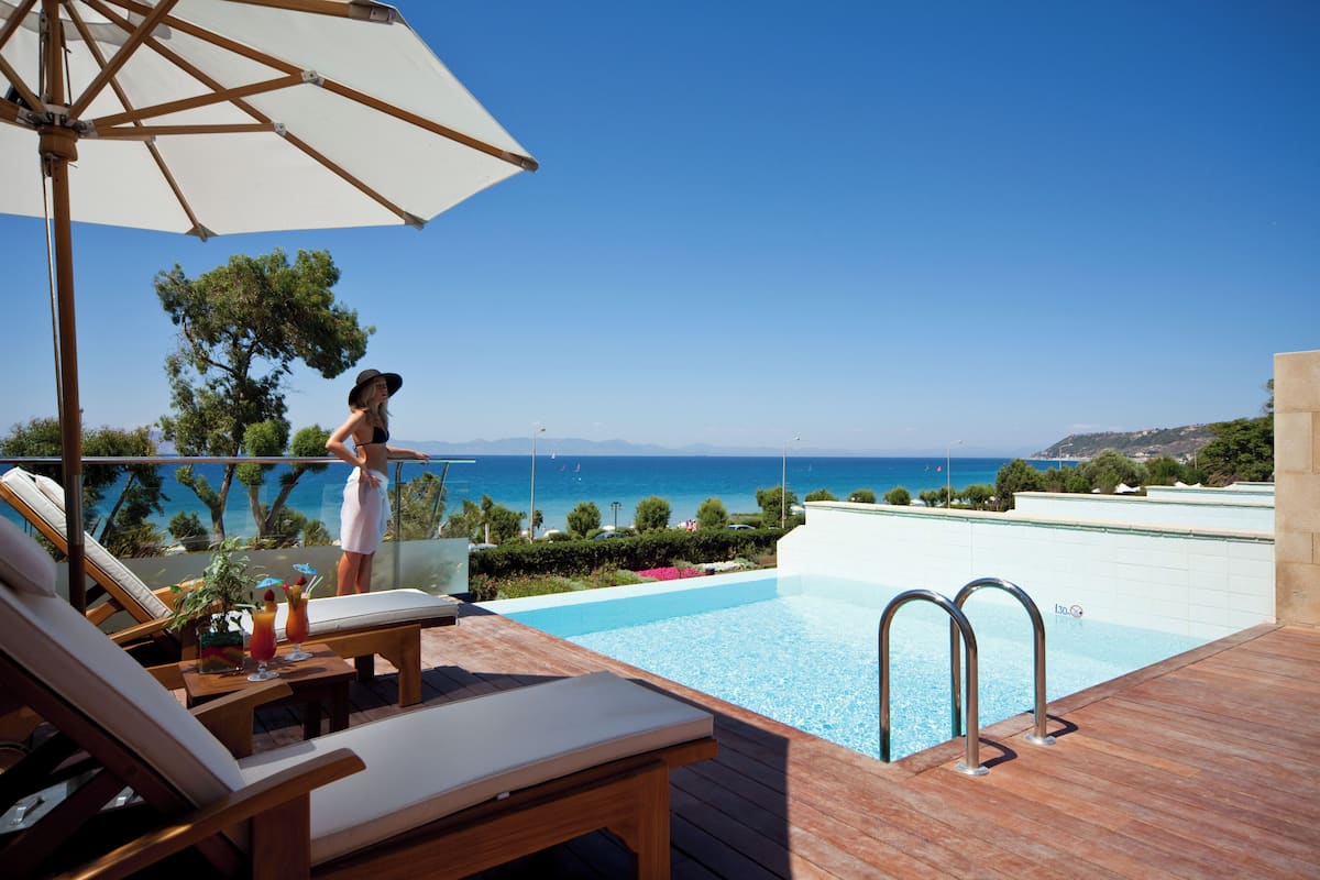 Uma área à beira da piscina com espreguiçadeiras, uma mesa com bebidas e vista para o mar.