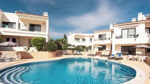 Piscina rodeada por espreguiçadeiras e guarda-sóis, sob um céu azul e límpido.