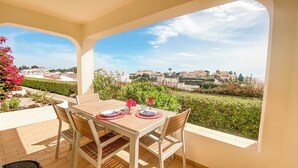 Varanda com mesa posta para dois, com vista para uma área residencial com sebes bem aparadas e casas.