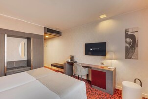 Quarto de hotel com cama, escrivaninha, televisão e cadeira.