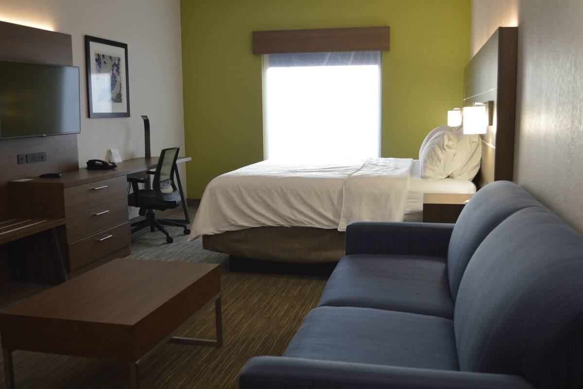 Quarto de hotel com cama, escrivaninha, cadeira, televisão e janela com vista.