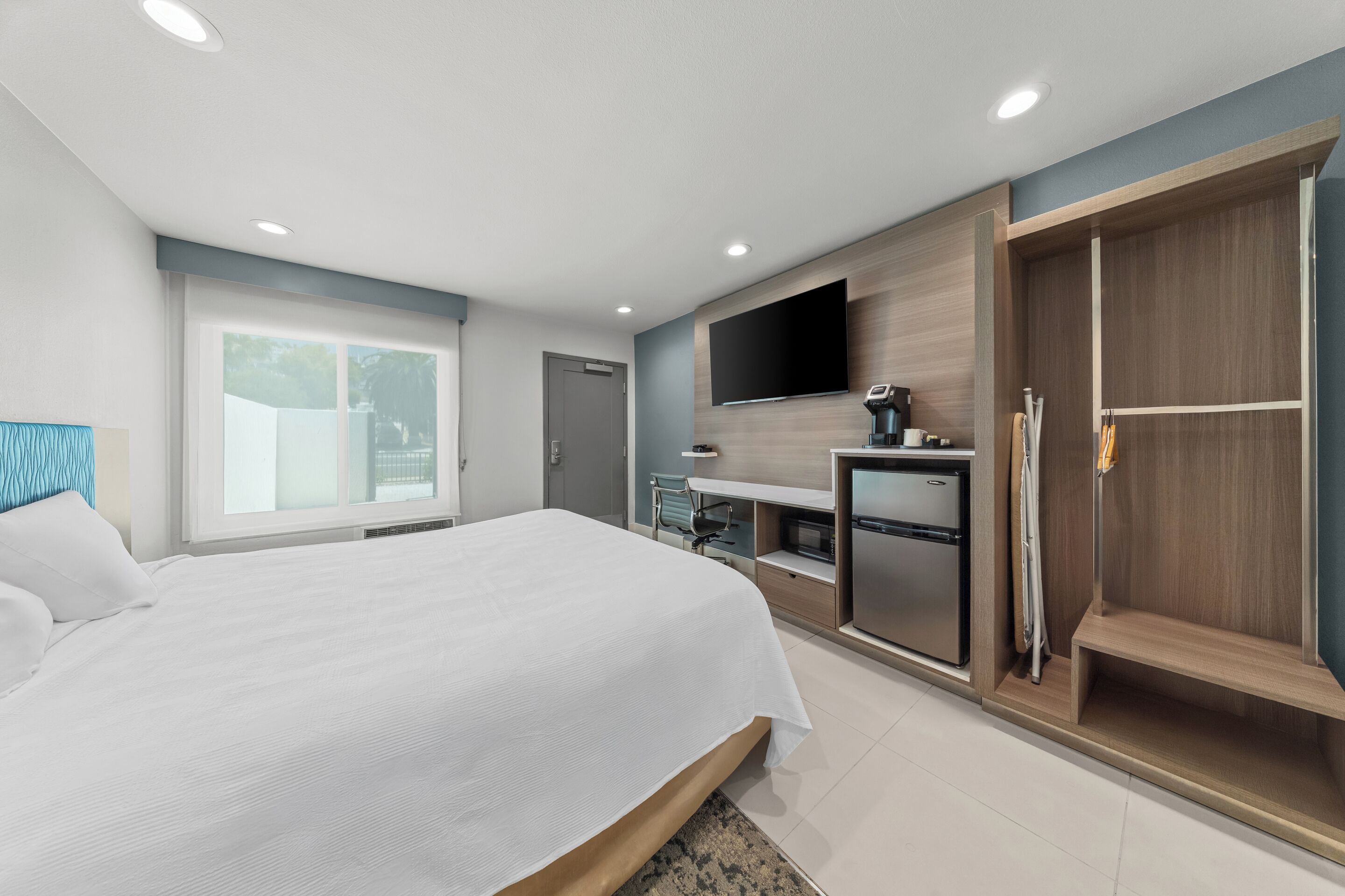 Quarto de hotel com cama grande, televisão na parede, minibar e closet espaçoso.