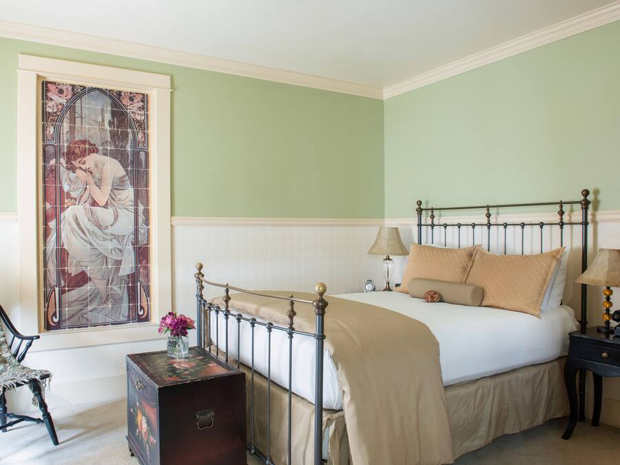 Quarto com cama, mesas de cabeceira, uma cadeira e um grande vitral.