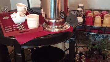 Uma área de cozinha com uma panela de aço inoxidável grande sobre uma mesa, toalha de mesa vermelha e diversos utensílios de cozinha, incluindo xícaras e uma tigela.
