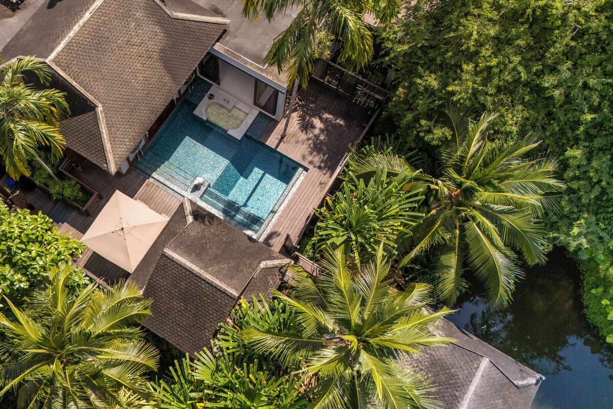 Vista aérea de um resort com piscina, palmeiras e um corpo de água.
