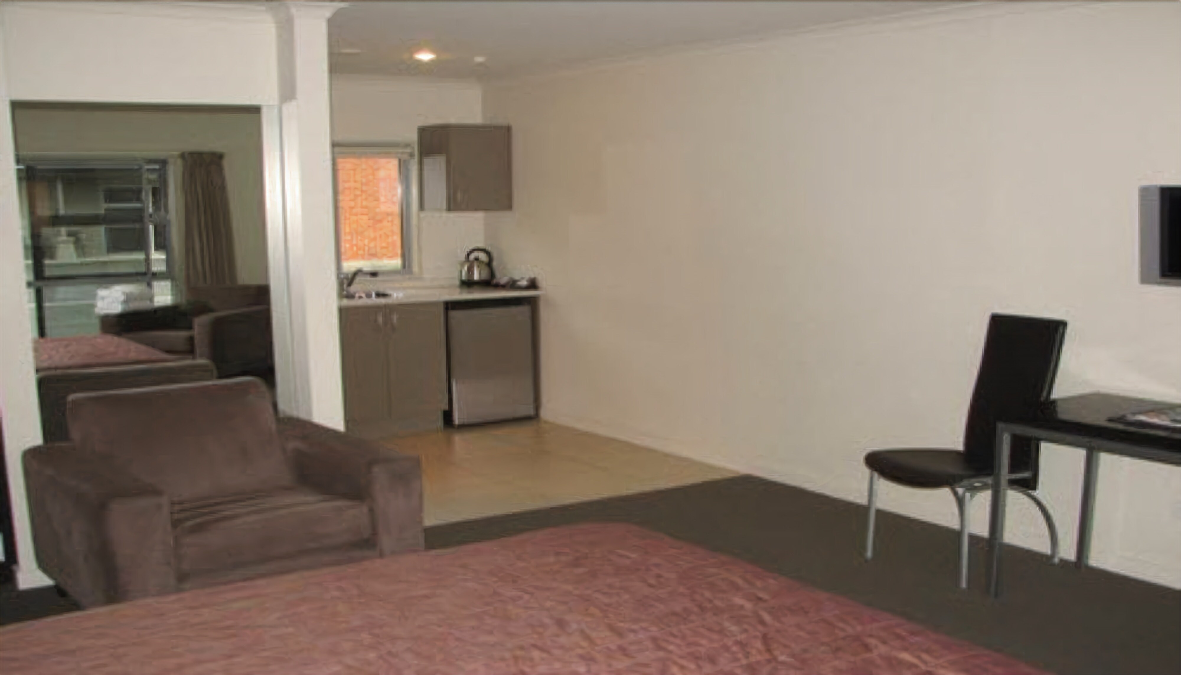 Quarto de hotel com cama, escrivaninha, cadeira, cozinha compacta e banheiro.