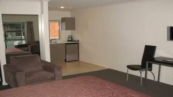 Quarto de hotel com cama, escrivaninha, cadeira, cozinha compacta e banheiro.