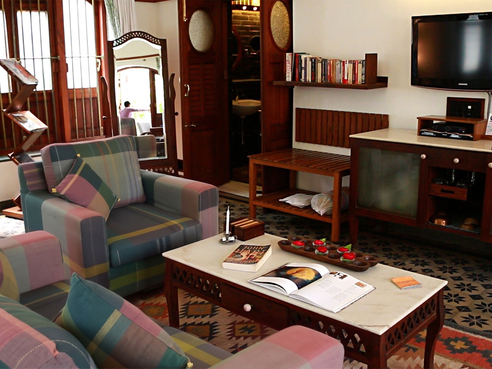 Uma sala de estar com sofá, mesa de centro e televisão. Há estantes de livros e um espelho decorativo.