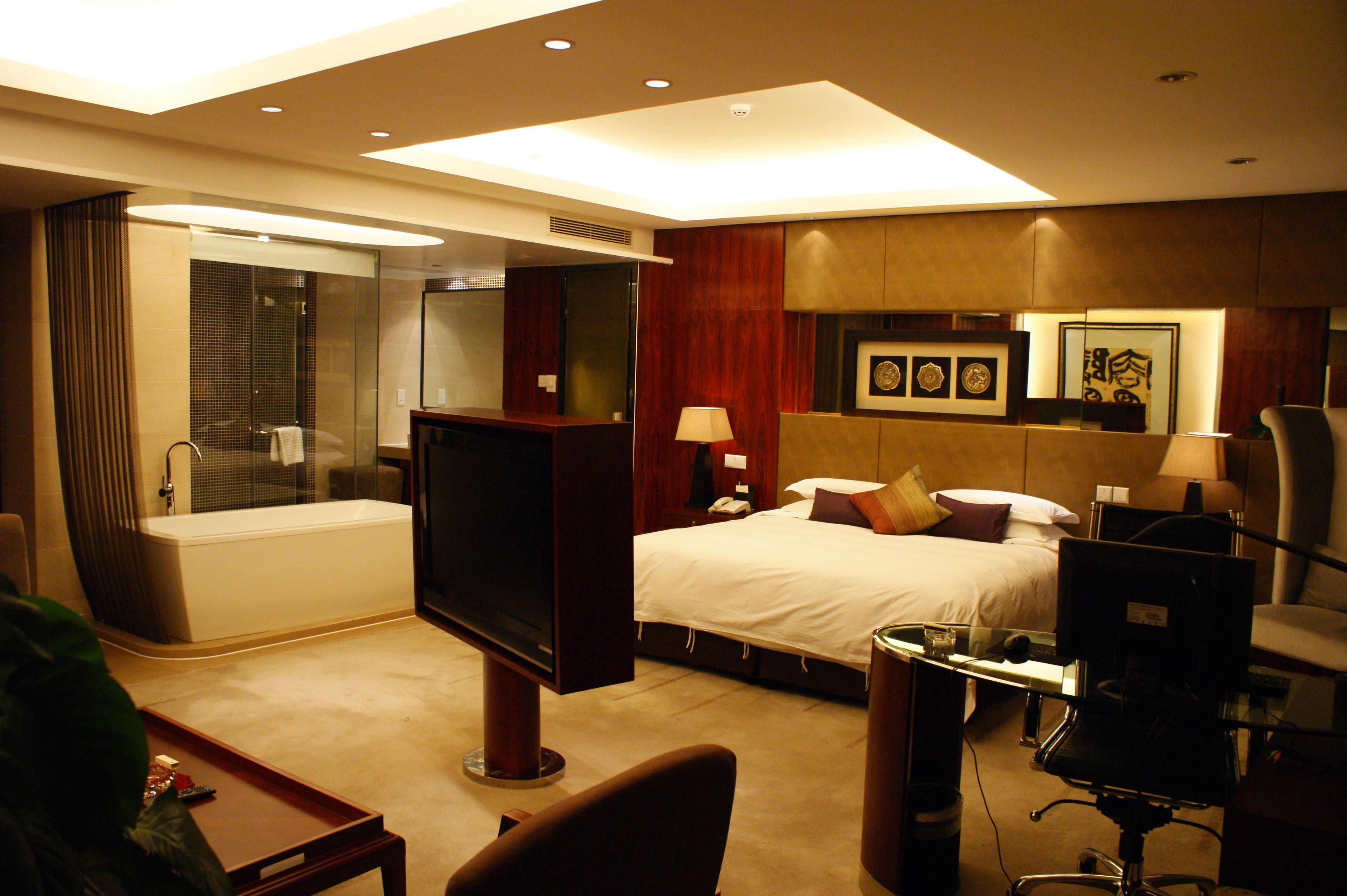 Quarto de hotel com uma cama grande, televisão, escrivaninha, cadeira, banheira e chuveiro.