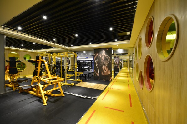 Uma academia com equipamentos de exercícios, uma parede de madeira com recortes circulares e um chão amarelo.