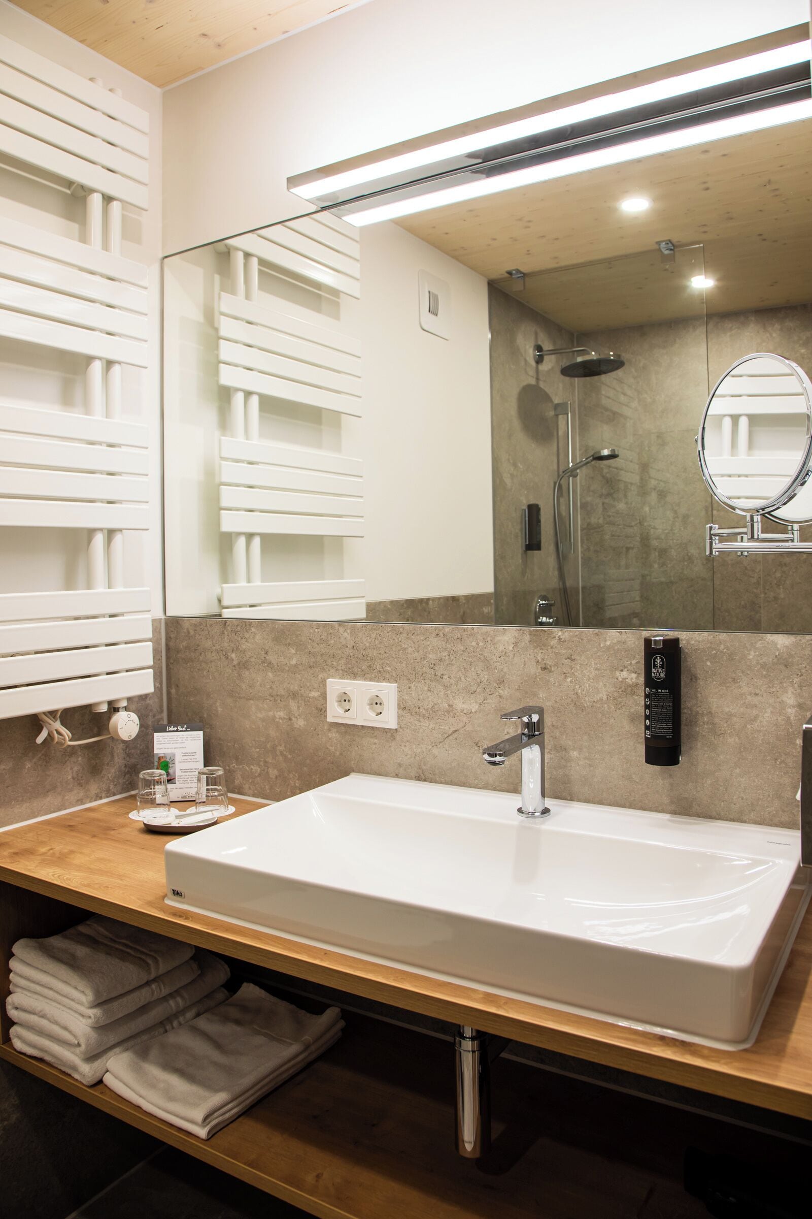 Uma casa de banho moderna com uma grande pia, espelho, porta-toalhas e zona de chuveiro.