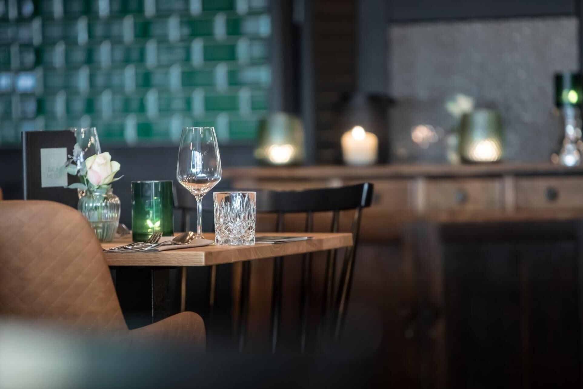 Uma mesa de jantar posta com taças de vinho, um vaso com flores e uma vela.