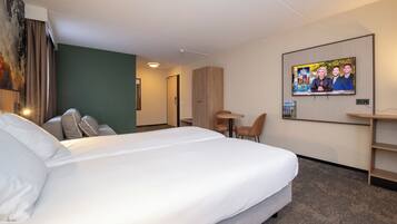 Quarto de hotel com cama grande, escrivaninha, cadeira, TV na parede e um quadro na parede.