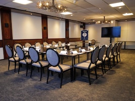 Uma sala de conferências com várias mesas e cadeiras, uma tela grande e um letreiro com a palavra 'Welcome'.