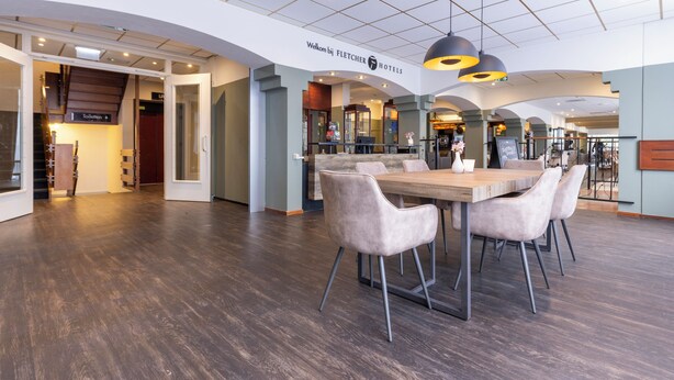 Um hall de hotel espaçoso com um balcão de atendimento de madeira, área de estar com poltronas estofadas e teto alto com padrão de grade.