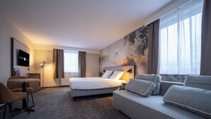 Quarto de hotel com cama, sofá, escrivaninha e televisão.