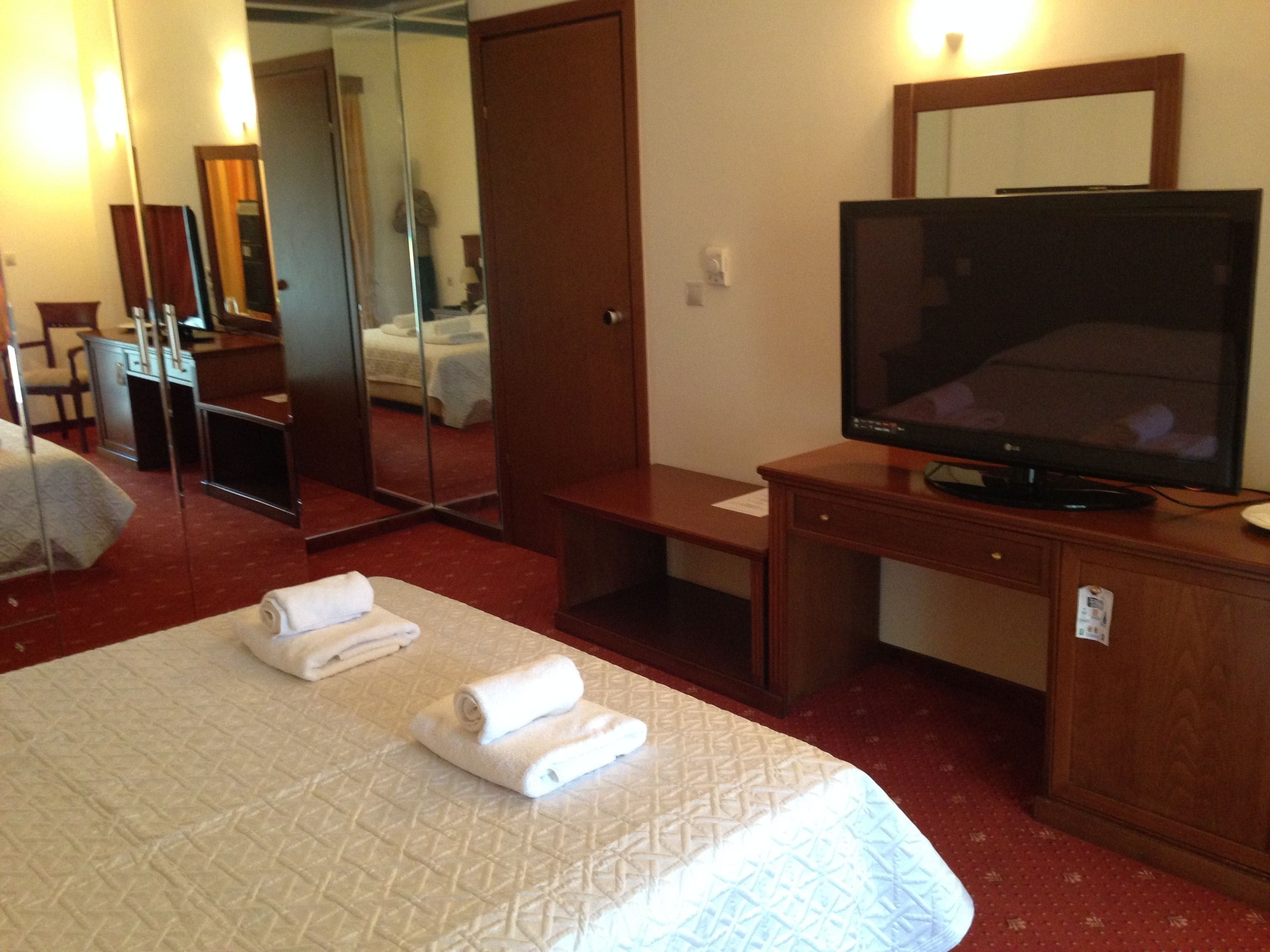 Quarto de hotel com cama, televisão, escrivaninha e espelho.